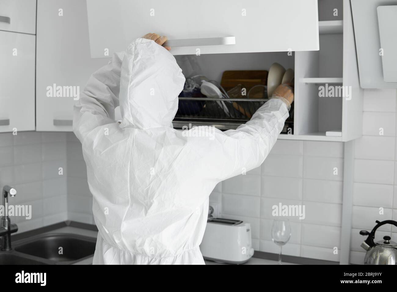 Man in white protective suit and in face medical mask cooks in the ...