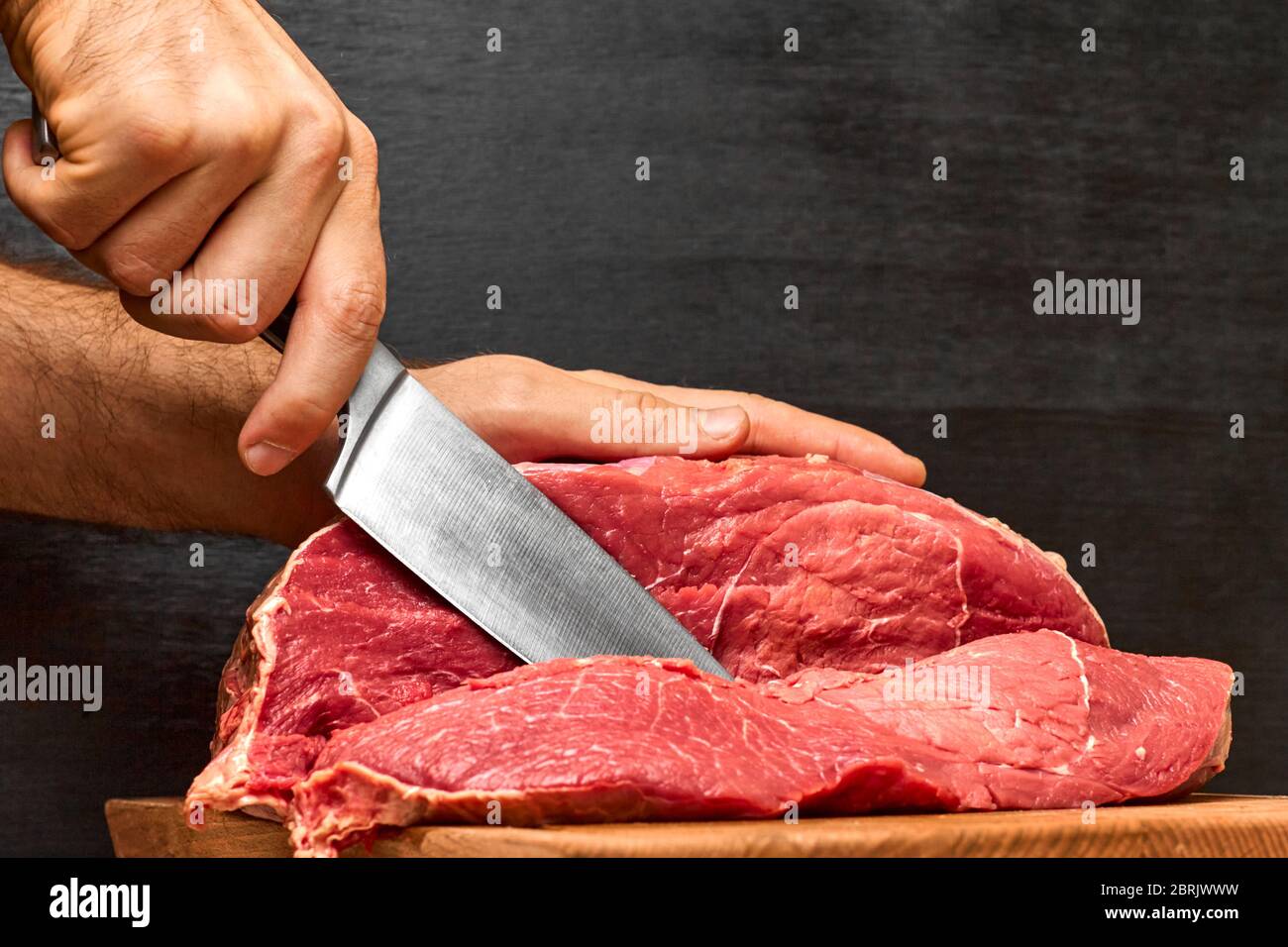 Closeup man hand cutting a beef meat with a knife on a black background ...