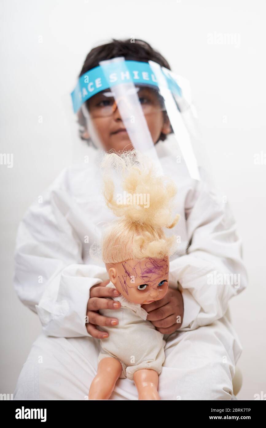 Sad Little girl with baby doll wearing protective face shield to stop ...