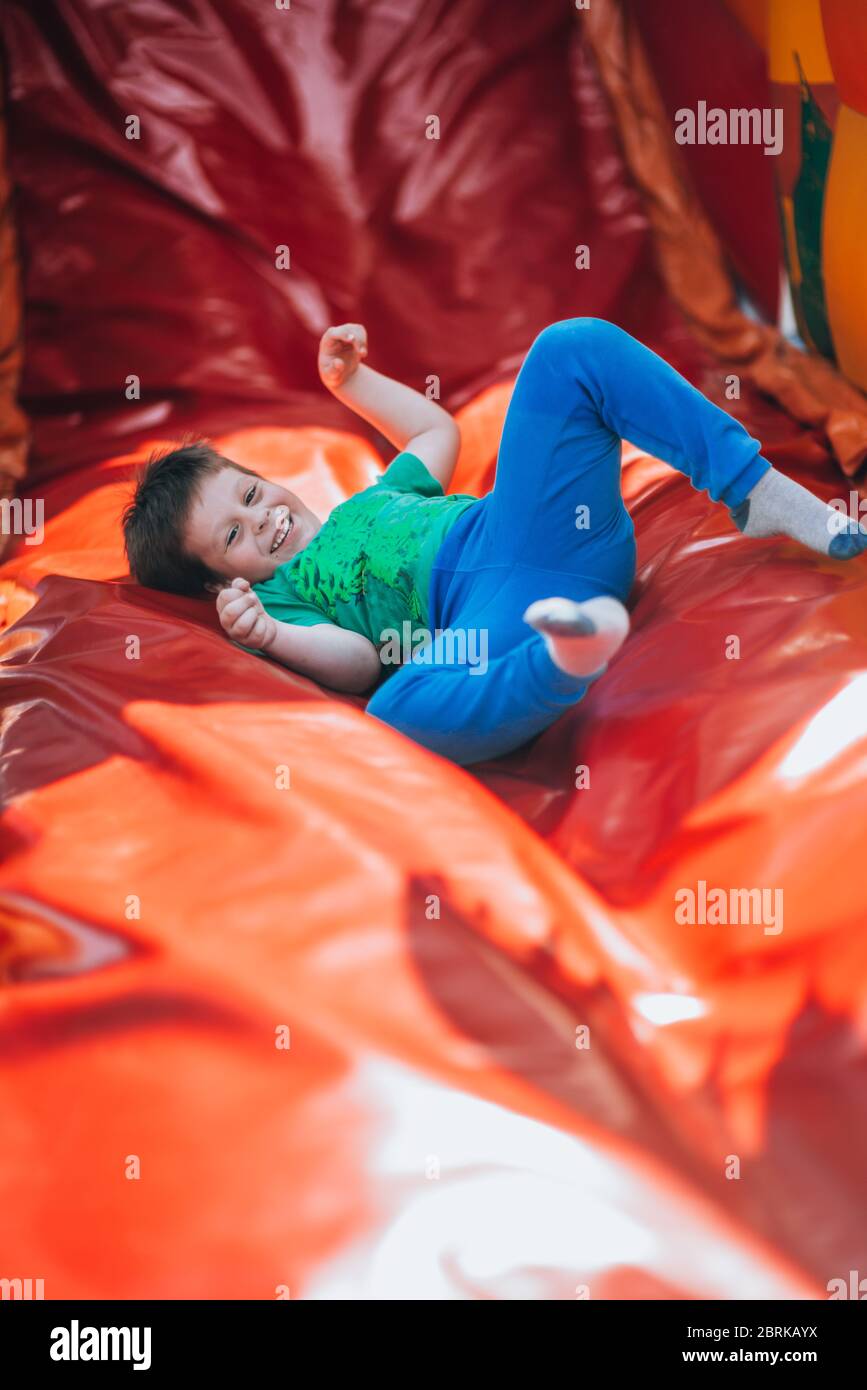Cute joyful smiling boy going for a slide on the big inflatable slide ...