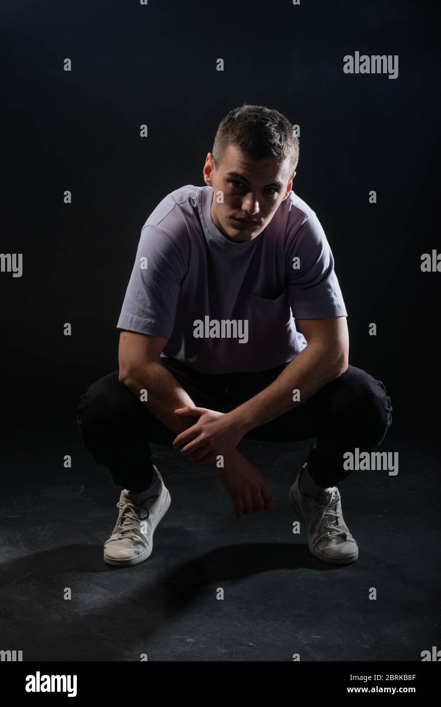 Male model squatting in a grey t-shirt isolated over a black background ...