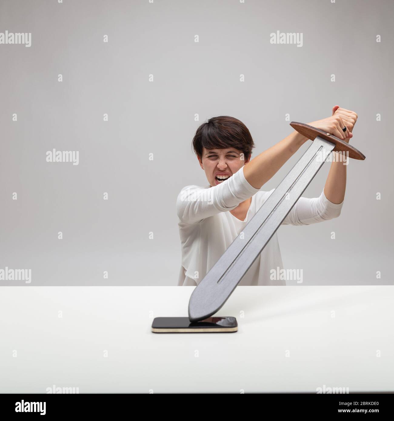 Angry woman attacking her mobile phone with a large toy sword with an ...