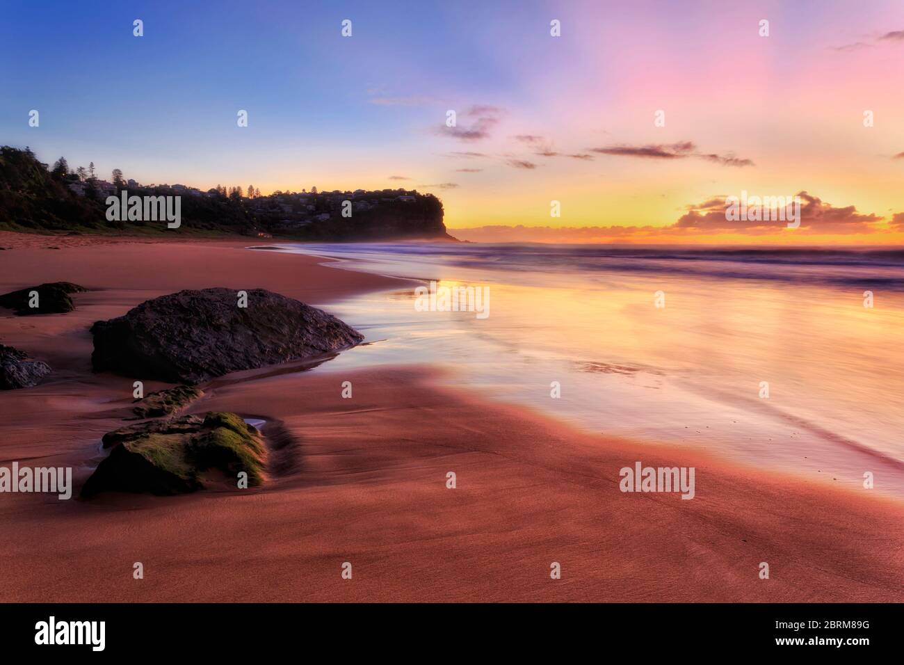 Smooth sand of Sydney Northern beaches at sunrise facing blurred waves ...