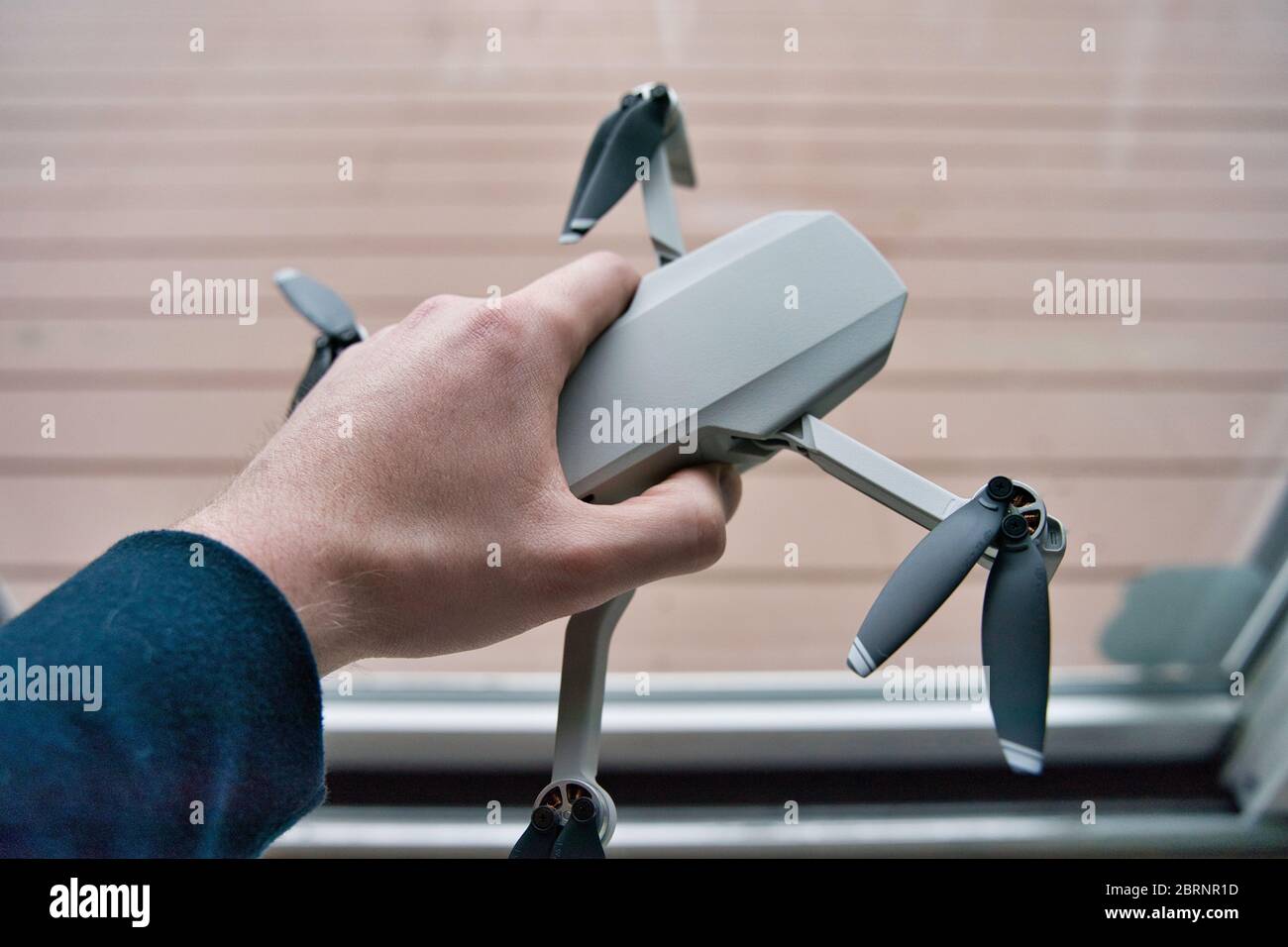 Hand holding drone with wooden deck visible in background. White man's ...