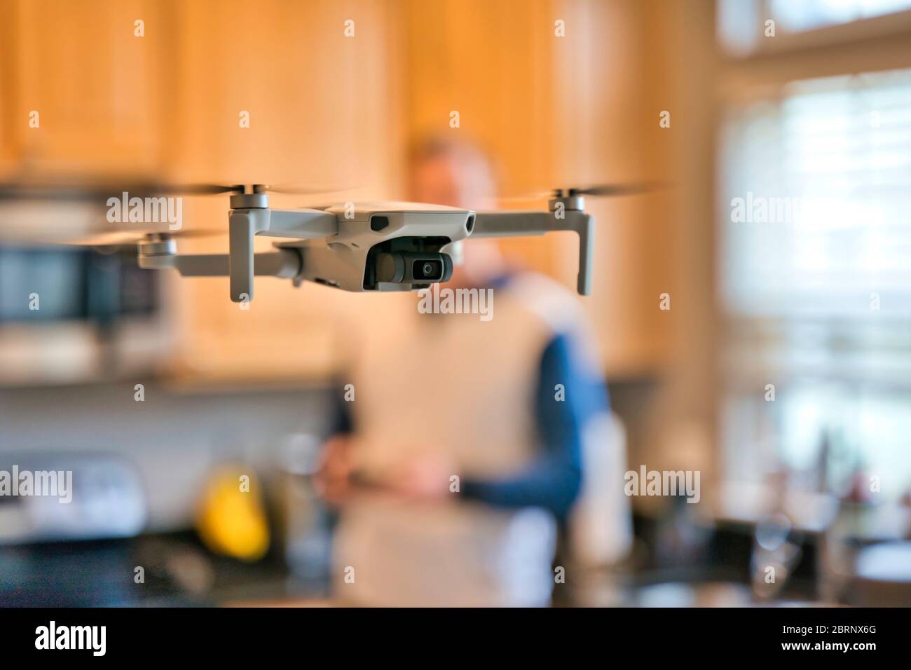 Drone flying indoors with kitchen and pilot visible in background ...