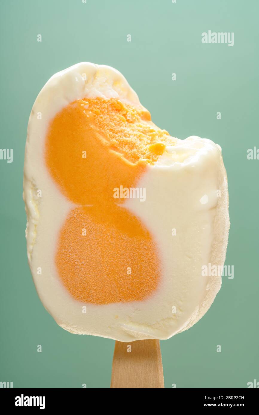 egg shape popsicle with a bite on green background Stock Photo - Alamy