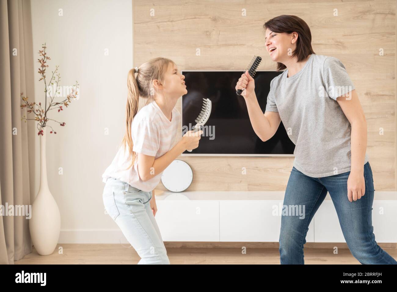 Happy family young adult mother and cute teen daughter having fun singing karaoke song in ...