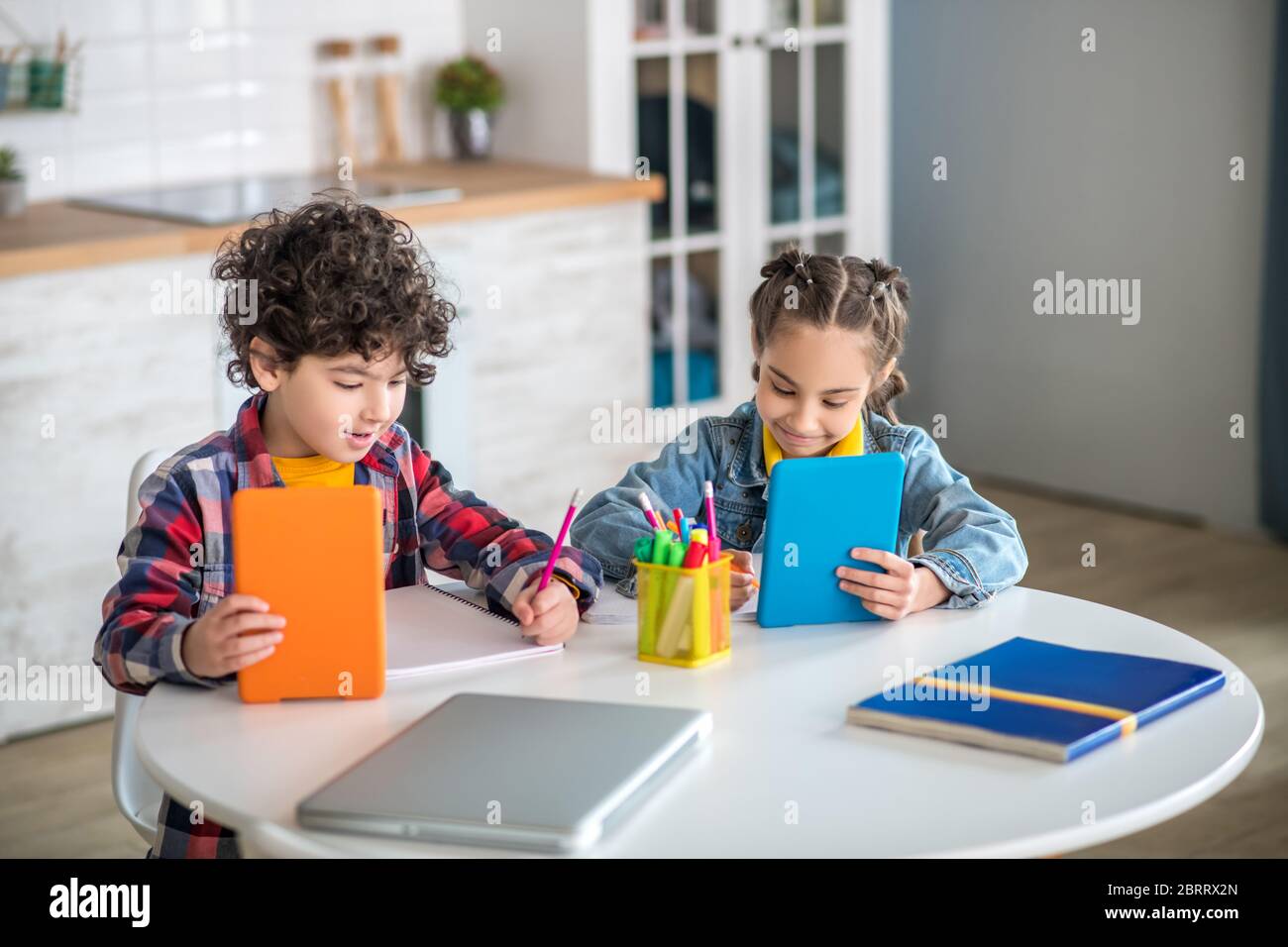 Boy and girl sitting at round table, holding tablets, writing Stock ...