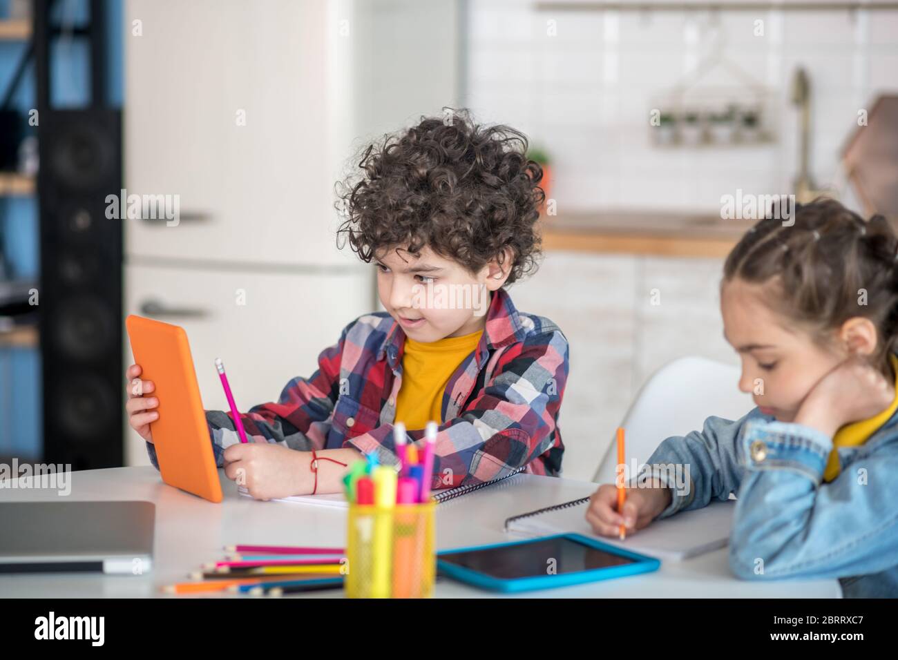 Boy and girl sitting at round table, holding tablets, busy with their ...