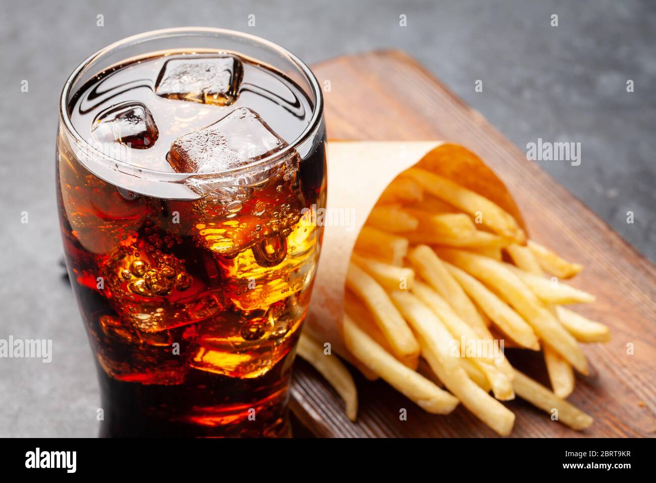 Glass of cola with ice cubes and potato fries chips. Fast food take ...