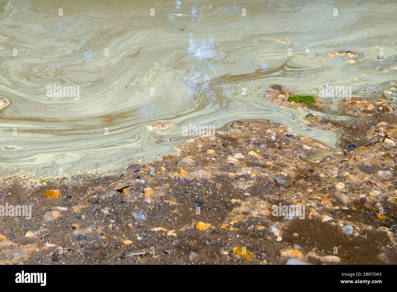 Dirty puddle on a broken road with yellow stains from pollen of plants ...