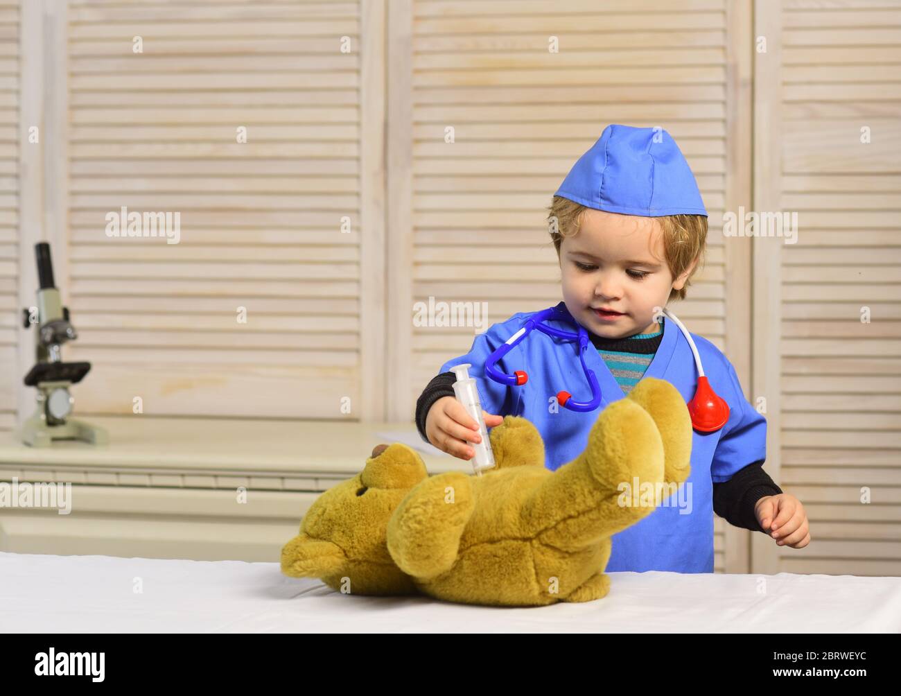 Boy in surgical uniform holds syringe on wooden background. Kid in ...