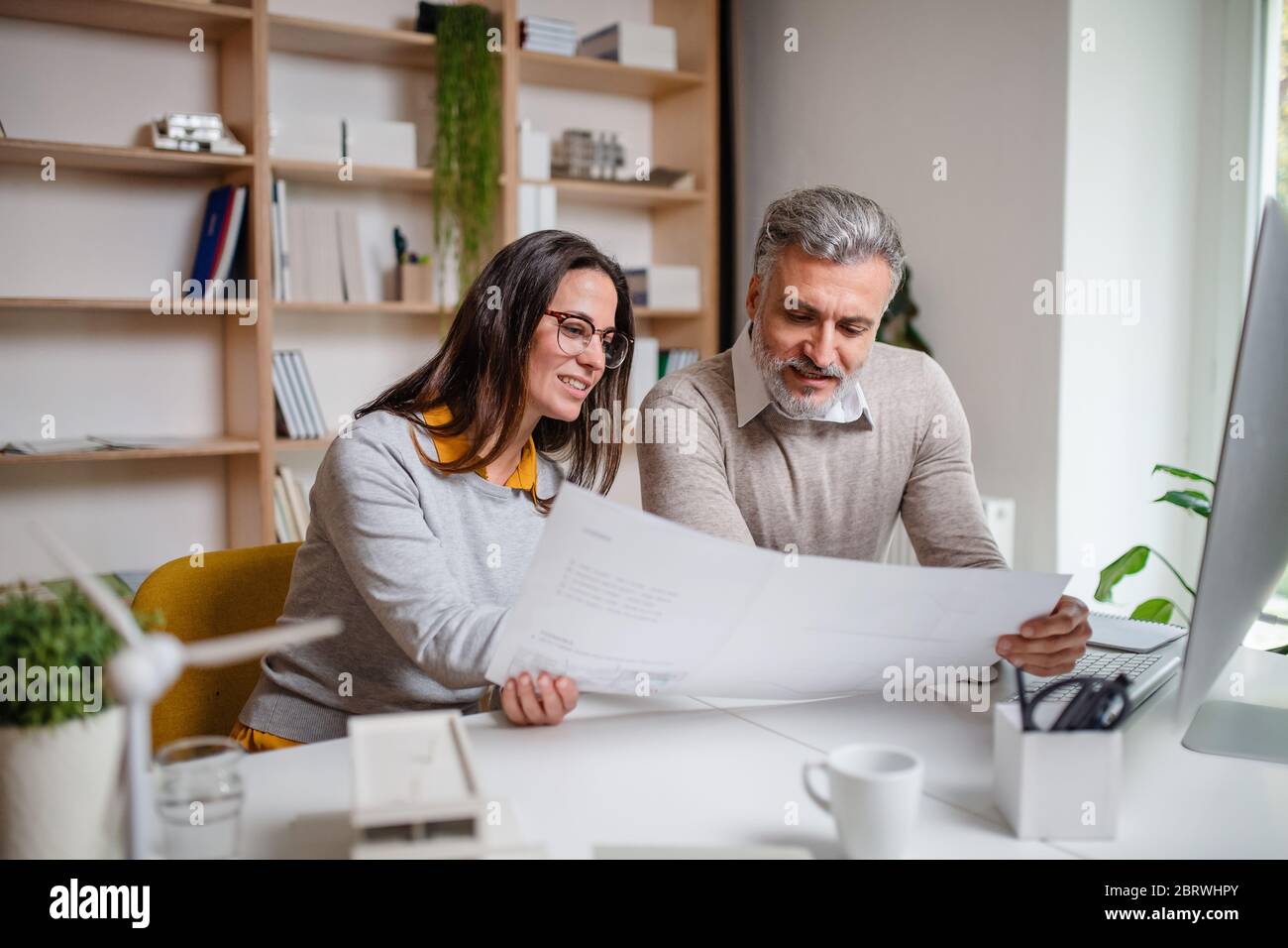 Architects sitting at the desk indoors in office, looking at blueprints ...