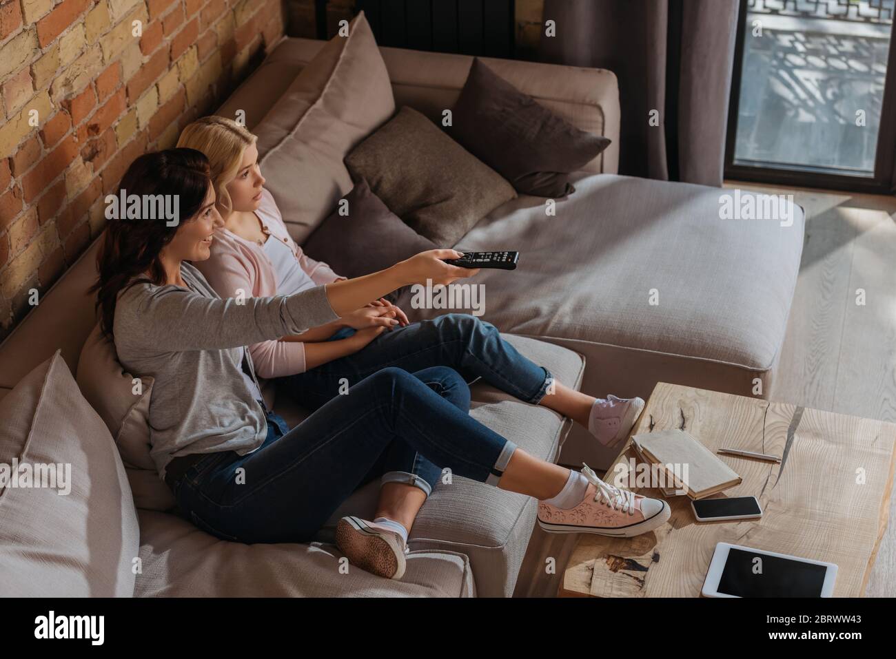 High angle view of smiling woman using remote controller near daughter ...
