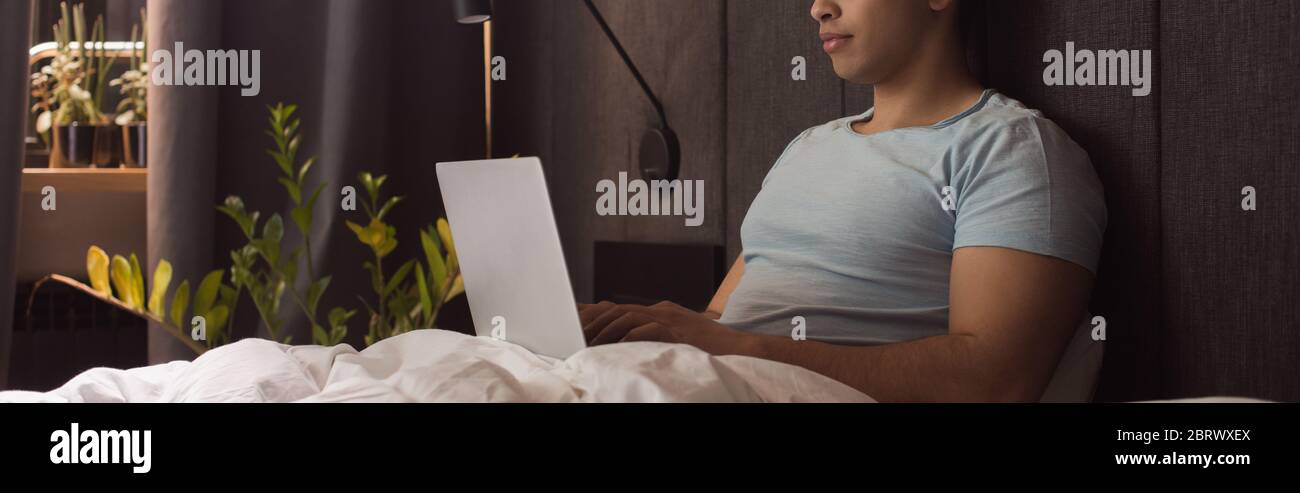 cropped view of mixed race man teleworking on laptop in bed during self ...