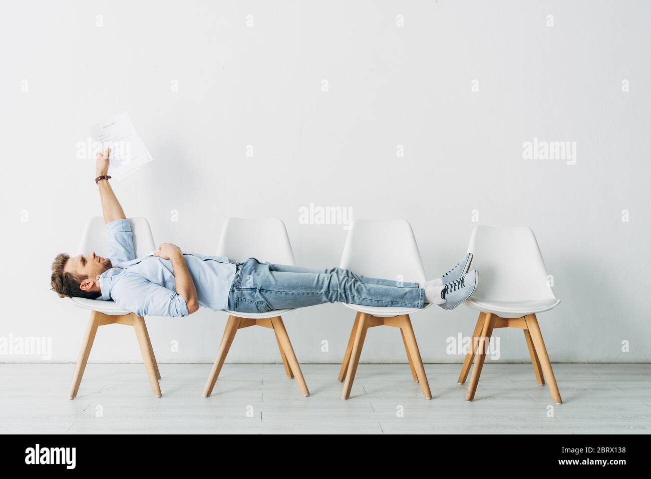 Side view of employee holding resume while lying on chairs in office ...