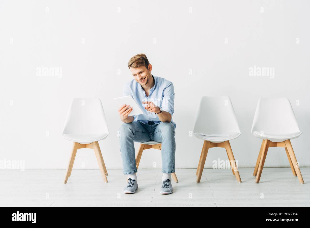 Smiling employee pointing with finger on digital tablet on chair in ...