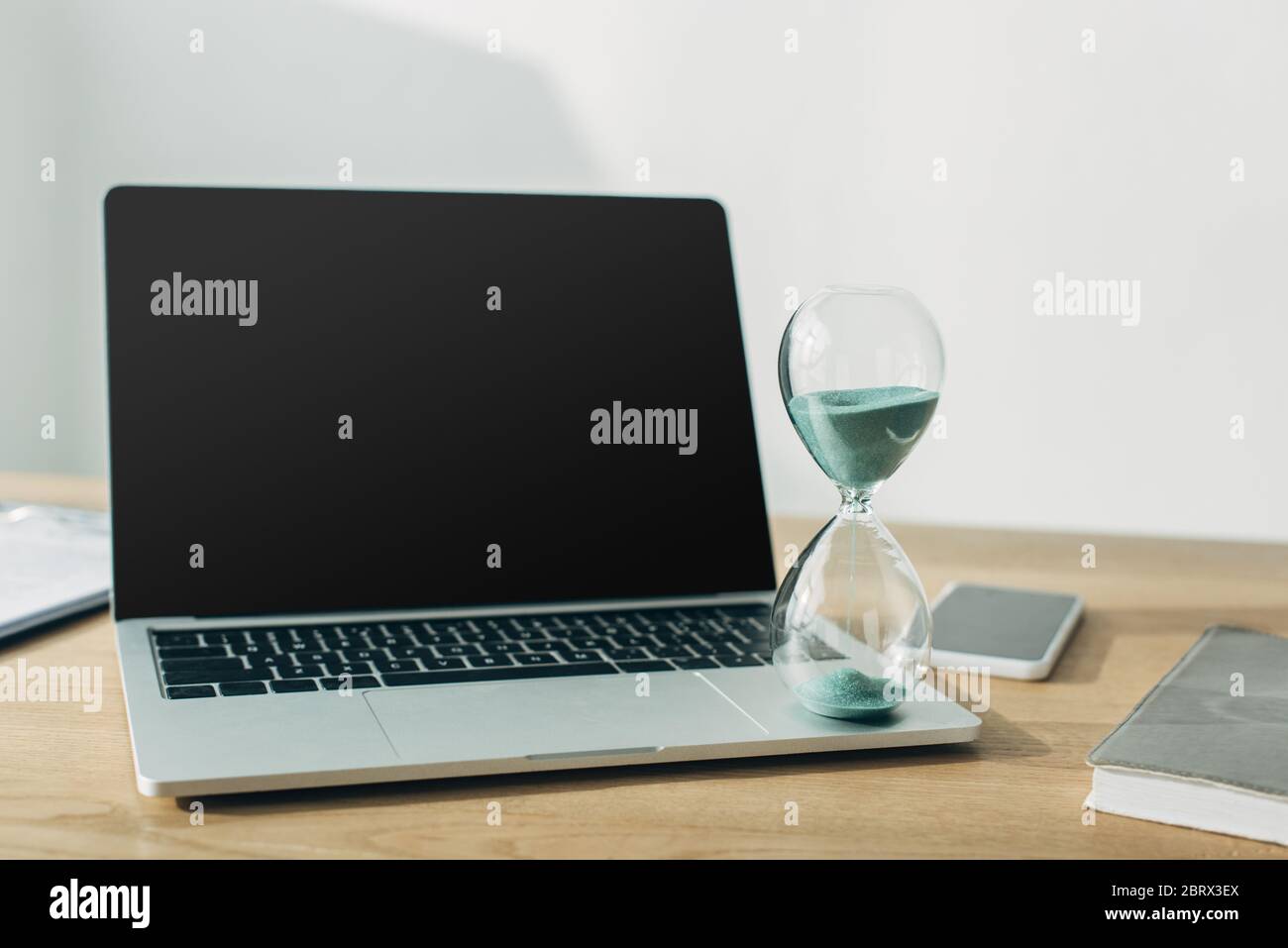 Hourglass on laptop with blank screen near smartphone and notebook on ...