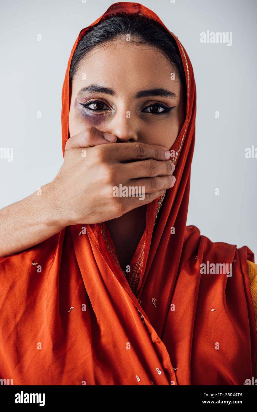 Male hand covering mouth to indian woman with bruise isolated on grey ...
