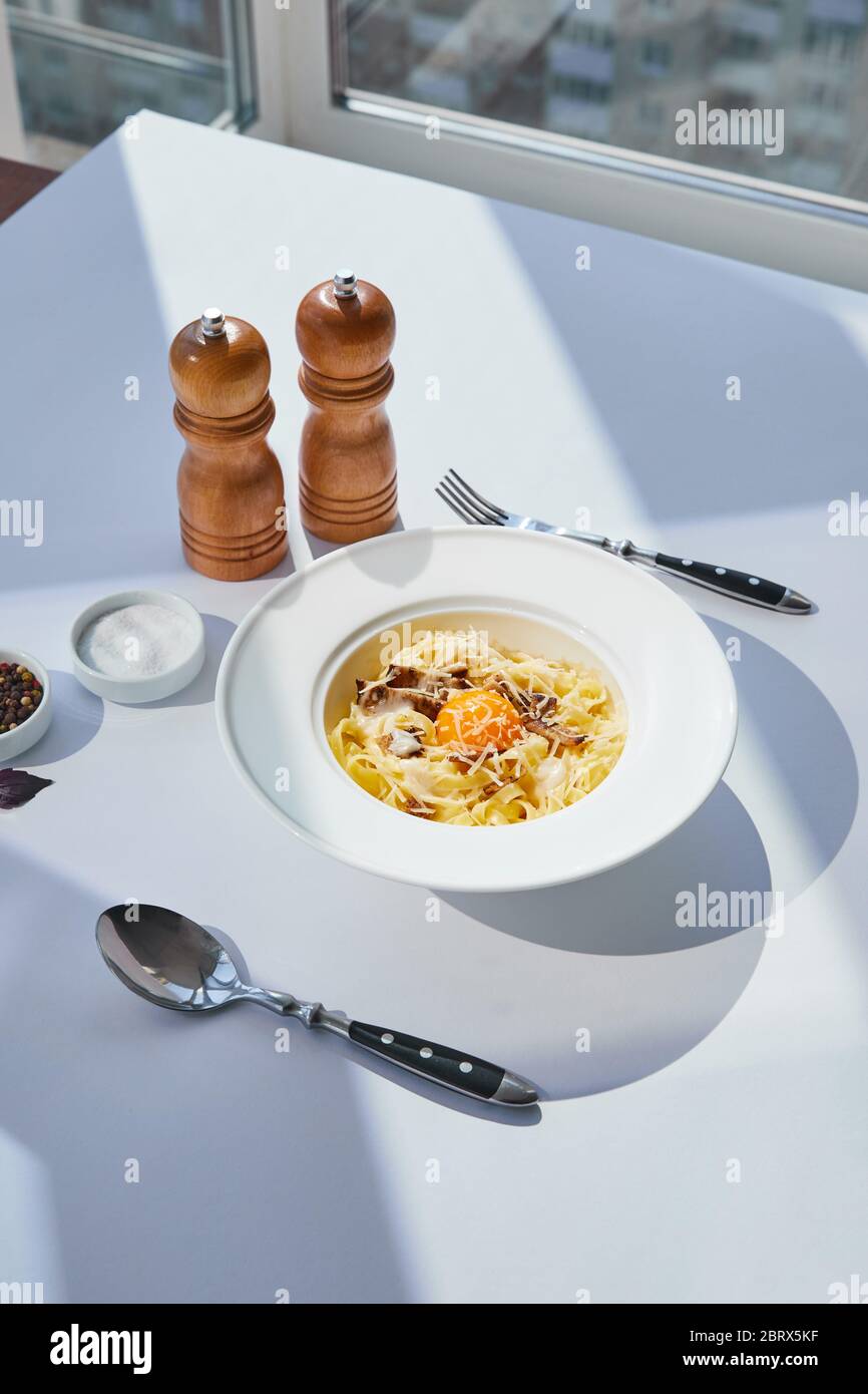 delicious pasta carbonara served with cutlery, salt and pepper mills on ...