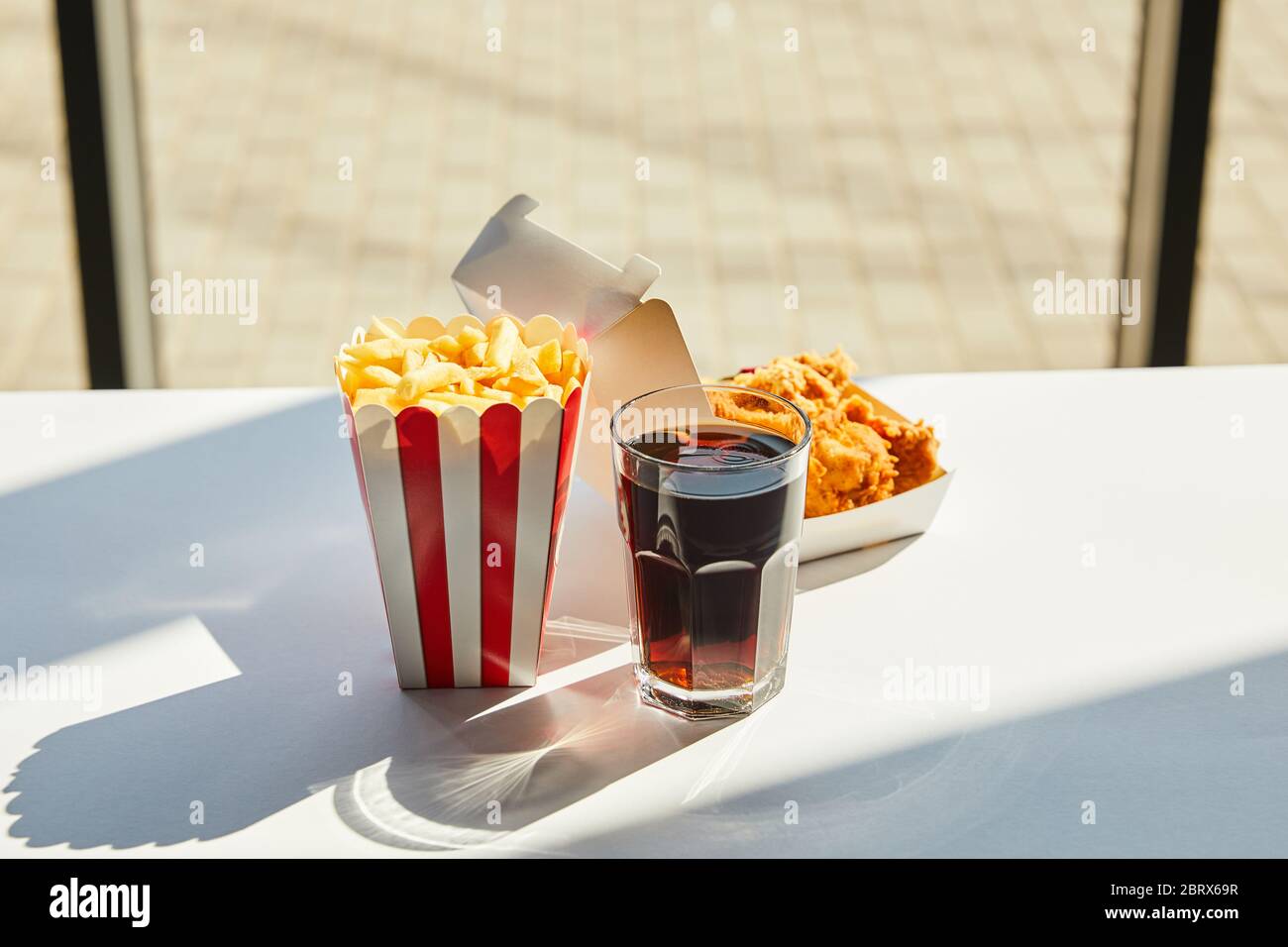 tasty deep fried chicken, french fries and soda in glass on white table ...