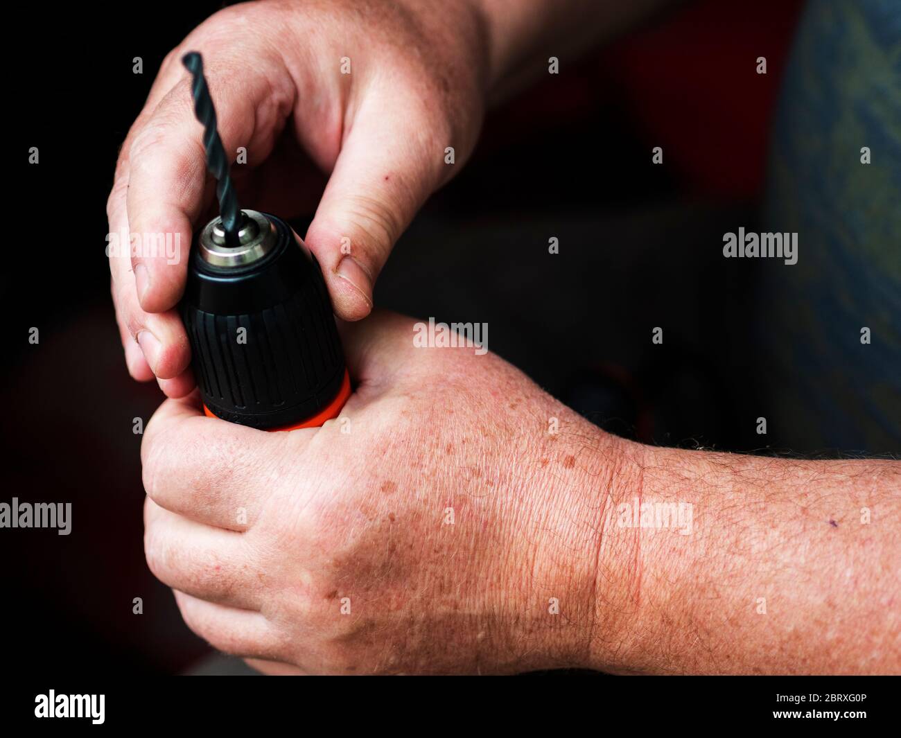 Hands of a Caucasian man inserts a drill into an electric drill chuck ...