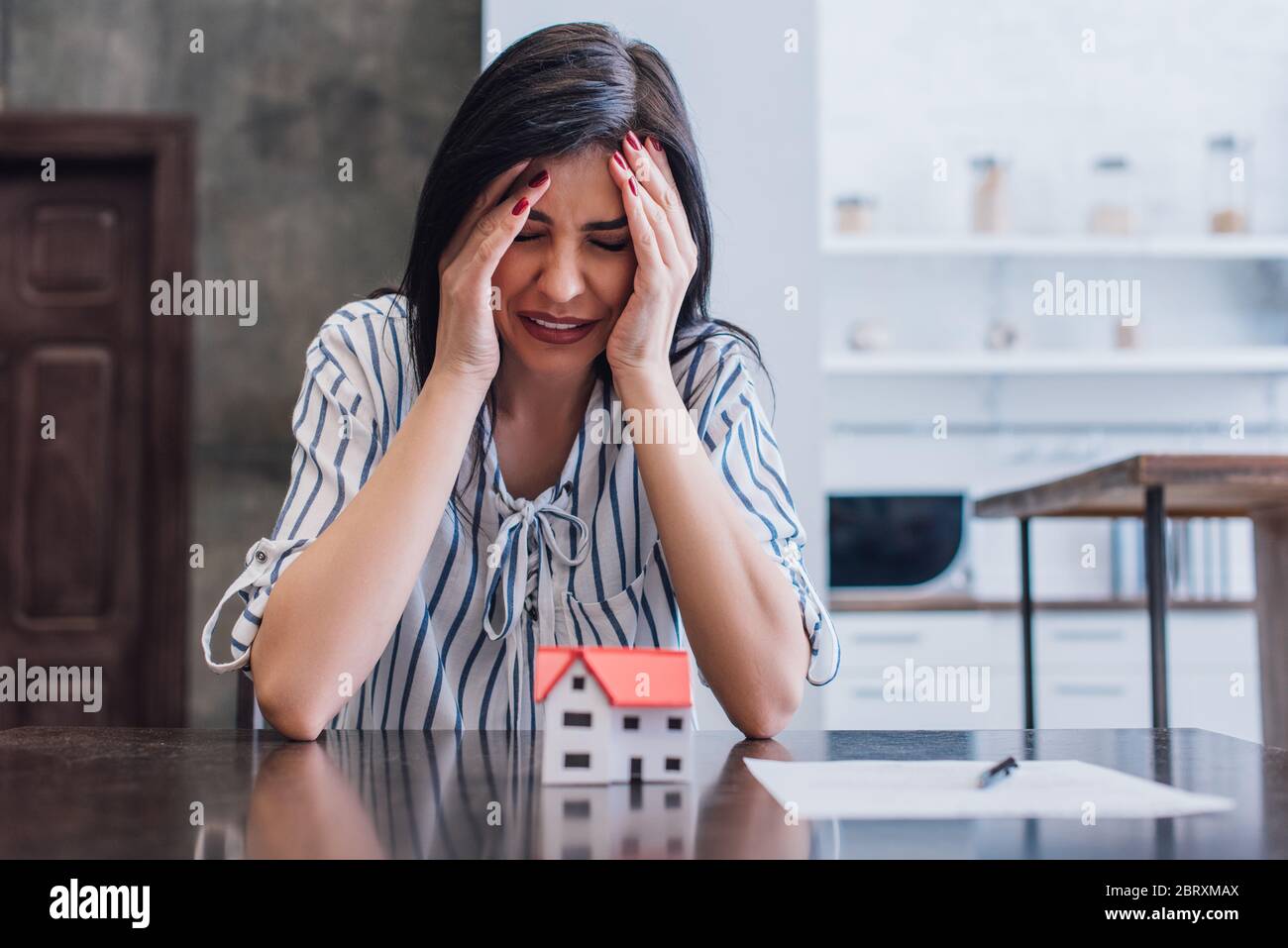 Upset woman crying at table with house model near document in room ...