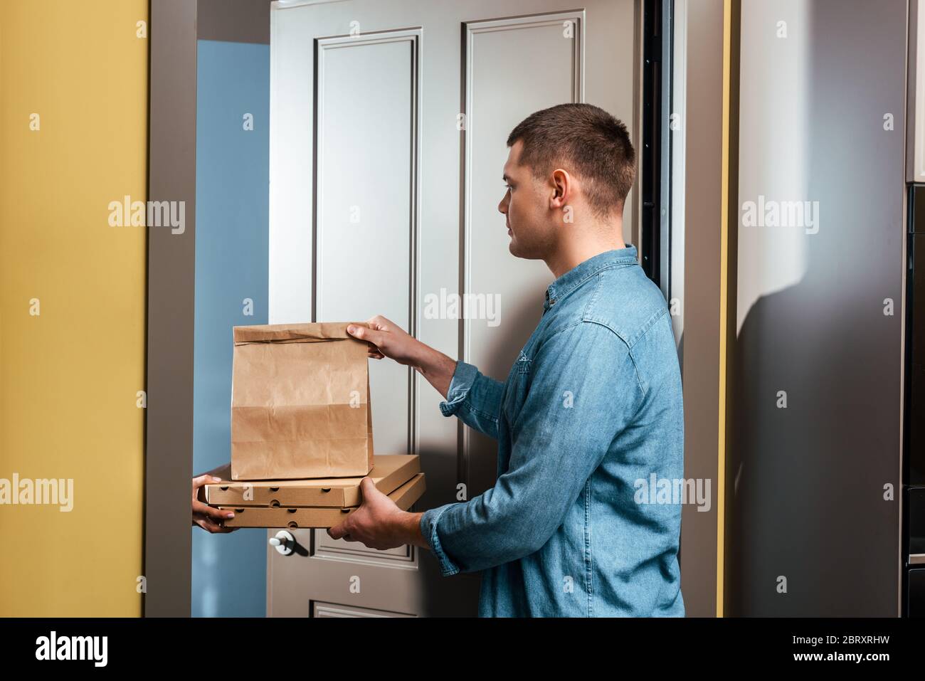 delivery man giving package to young man near open door at home Stock ...