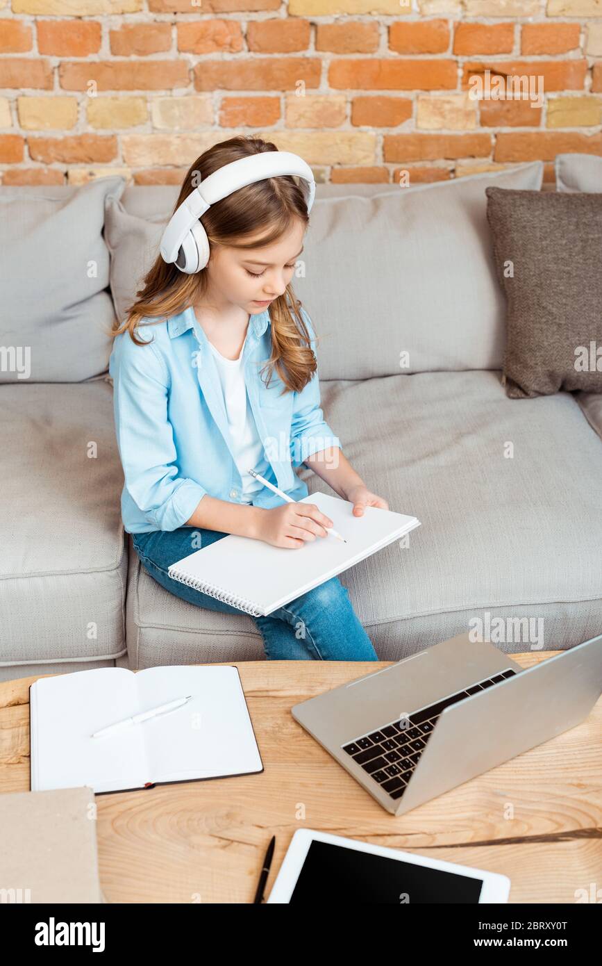 cute kid in headphones writing in notebook near gadgets Stock Photo - Alamy