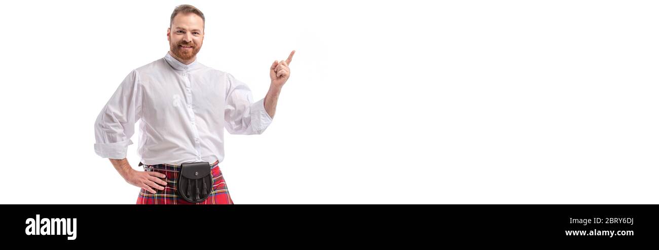 smiling Scottish redhead bearded man in red tartan kilt pointing with ...