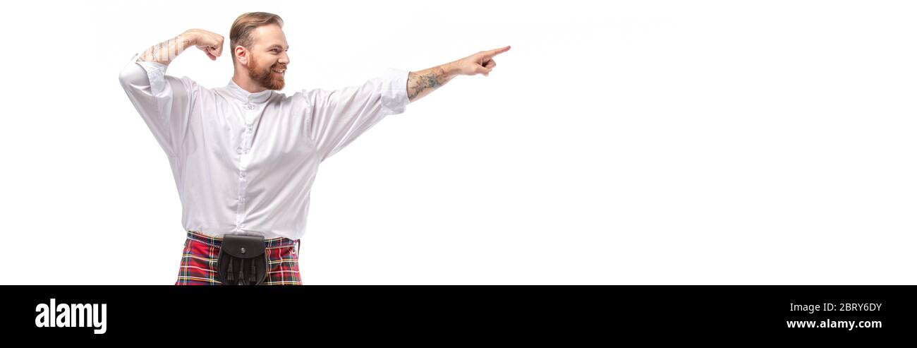 happy Scottish redhead man in red kilt pointing with finger aside ...