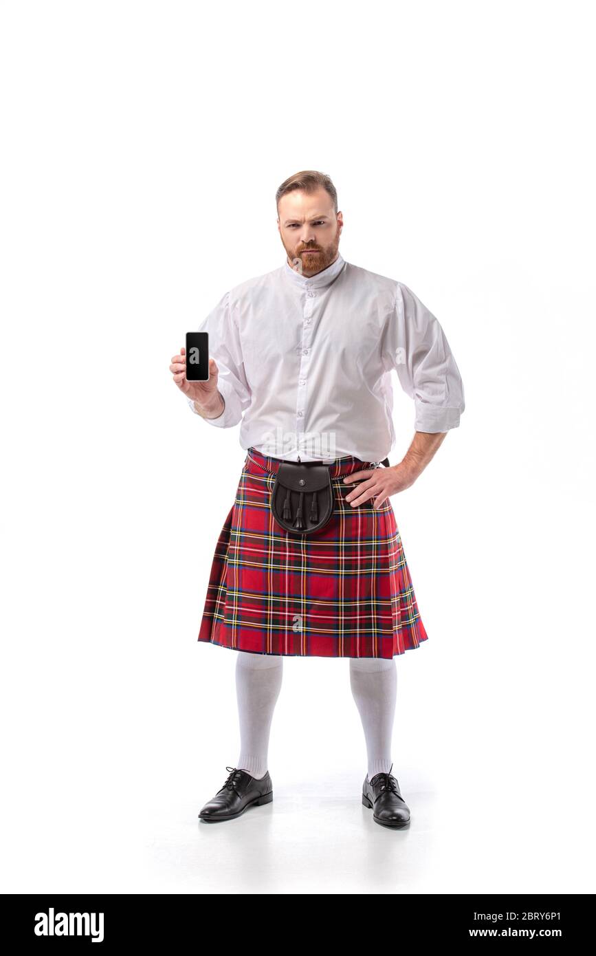 serious Scottish redhead man in red kilt holding smartphone with blank ...
