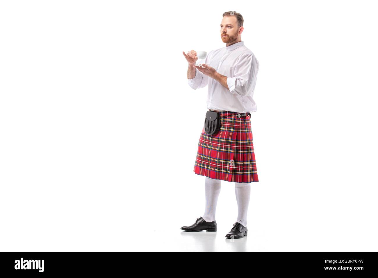 Scottish redhead man in red kilt drinking coffee on white background ...