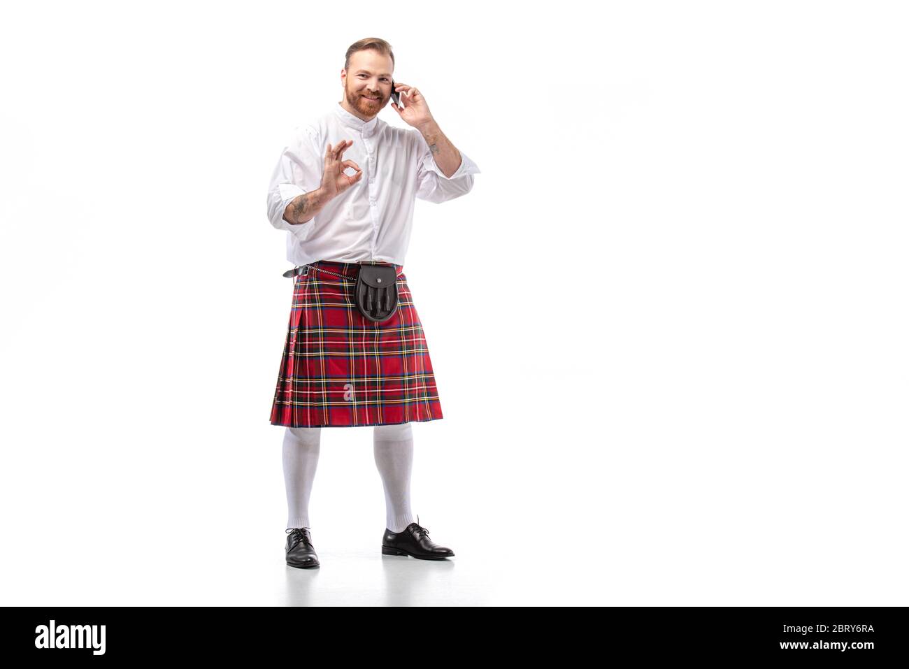 happy Scottish redhead man in red kilt talking on smartphone and ...