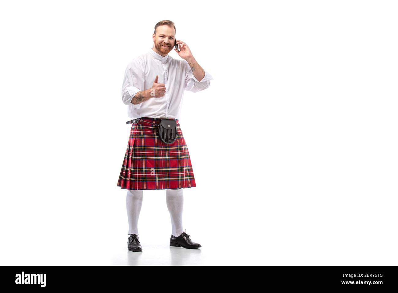 happy Scottish redhead man in red kilt talking on smartphone and ...