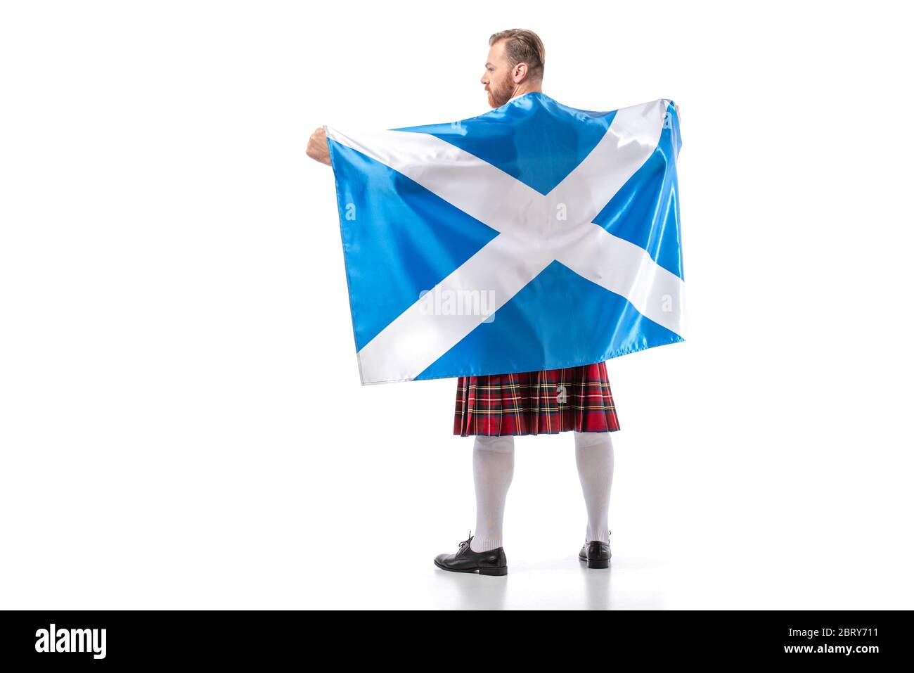 back view of Scottish redhead man in red kilt with flag of Scotland on ...