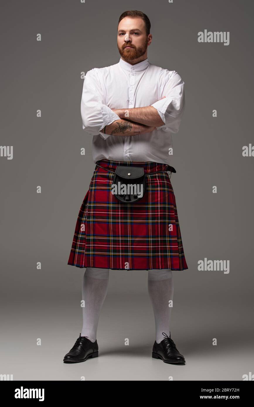 Scottish redhead man in red kilt with crossed arms on grey background ...