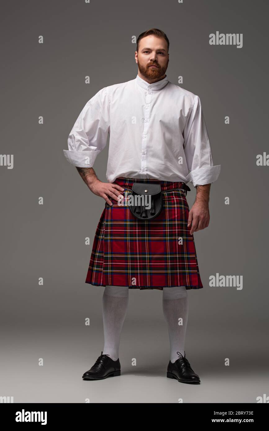 Scottish redhead man in red kilt with hand on hip on grey background ...