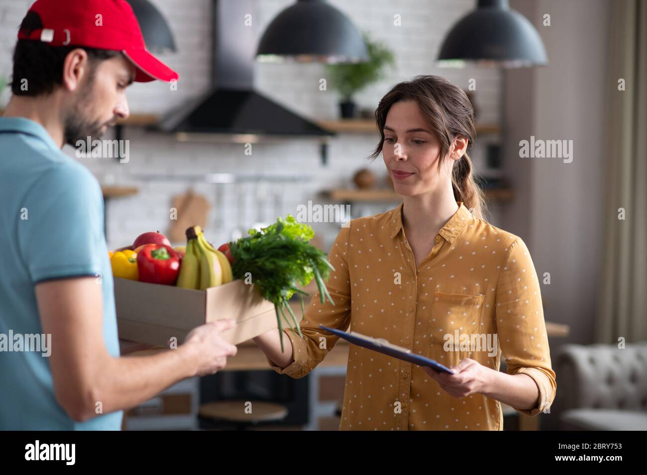 Dark-haired customer receiving groceries delivered by the courrier and ...