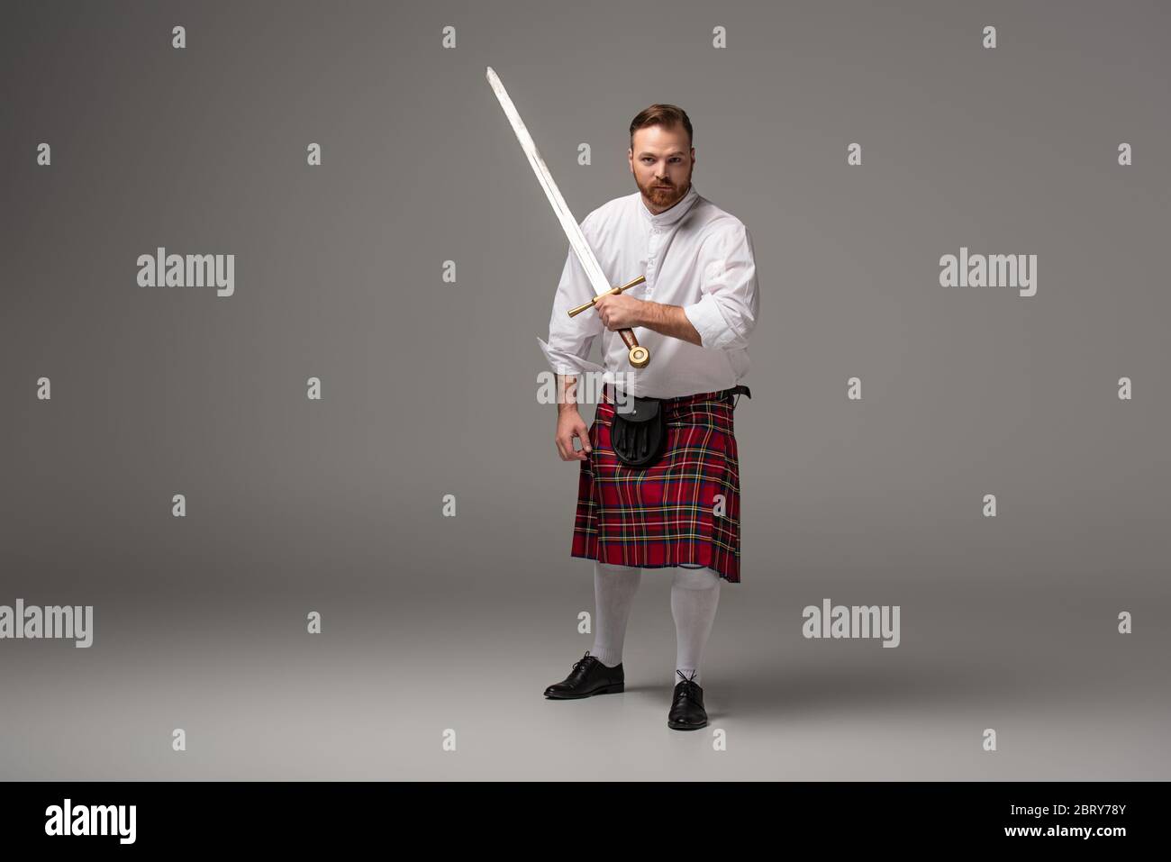 Scottish redhead man in red kilt with sword on grey background Stock ...