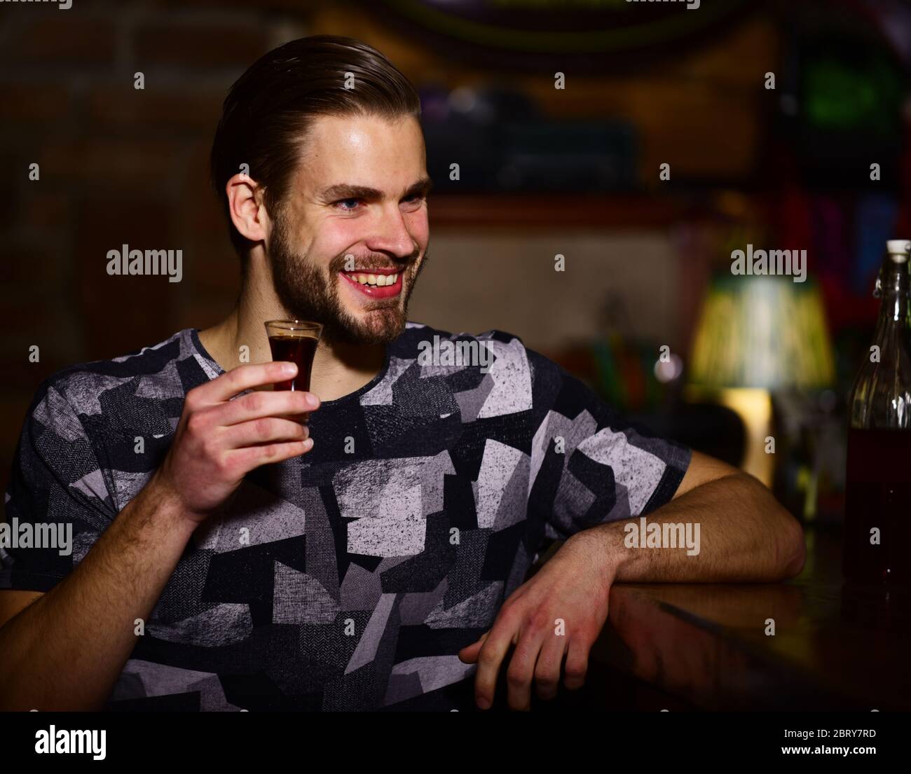 Macho with smiling face sits in bar and drinks alcohol. Guy at bar ...