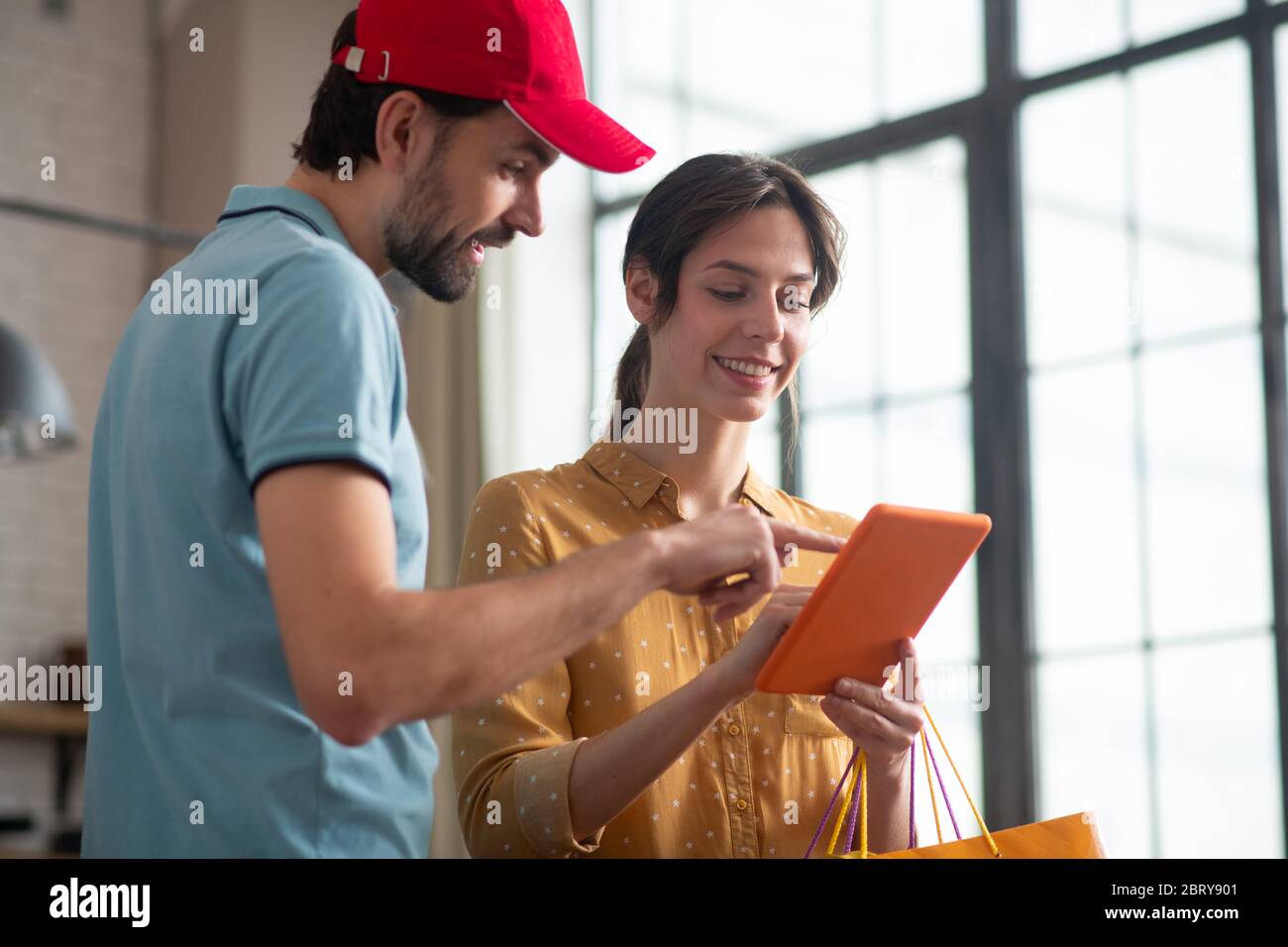 Deliver person in a red hat showing something on a tablet to a female ...