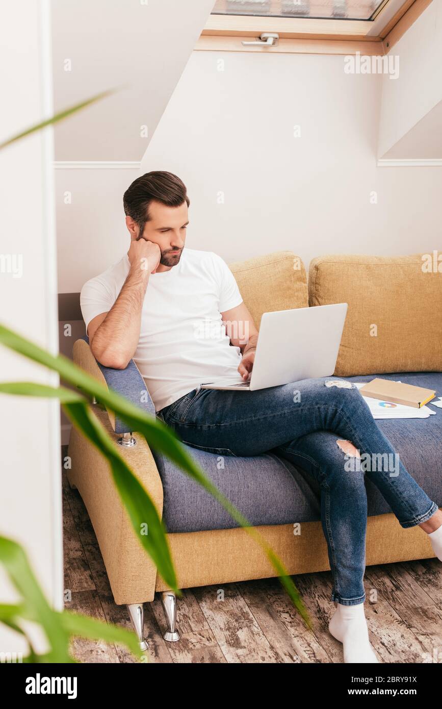 Selective focus of handsome teleworker using laptop near documents on ...