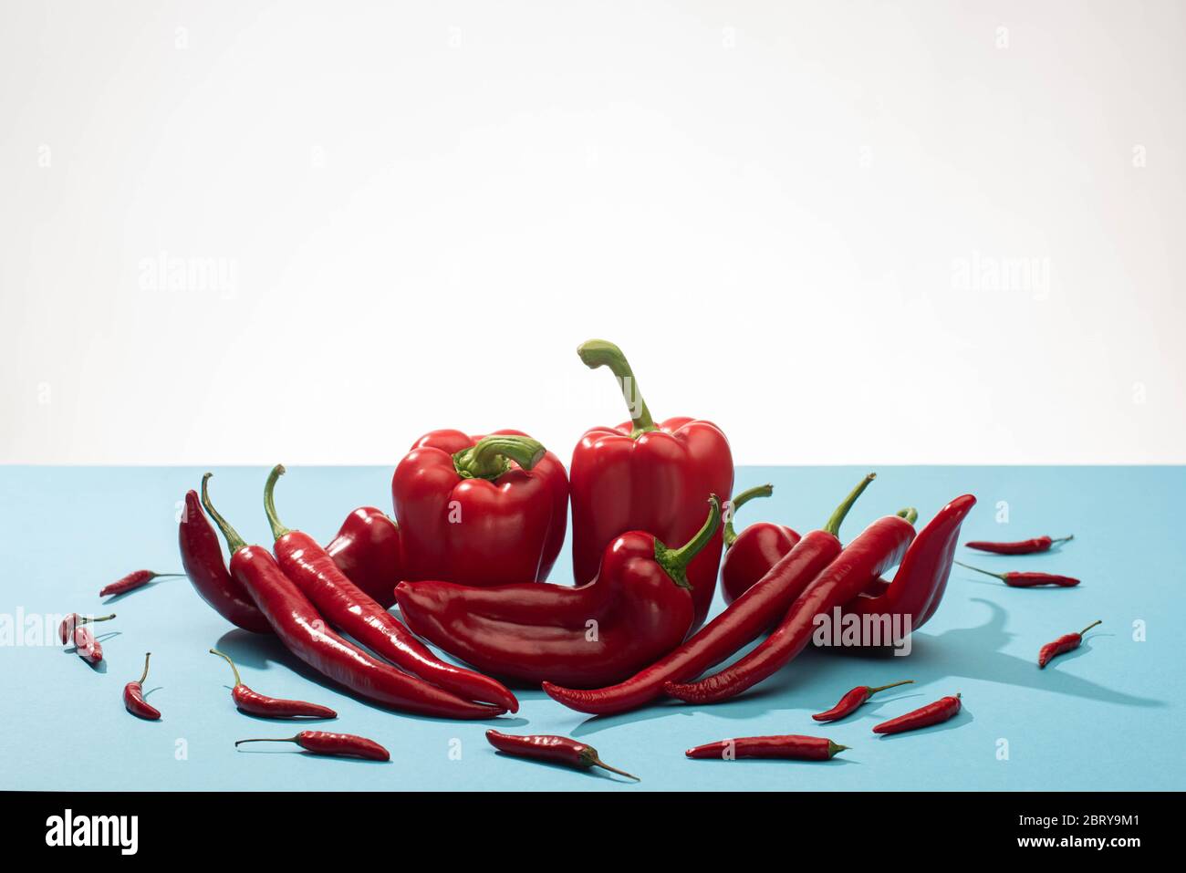 fresh red bell peppers and chili on blue surface on white background ...