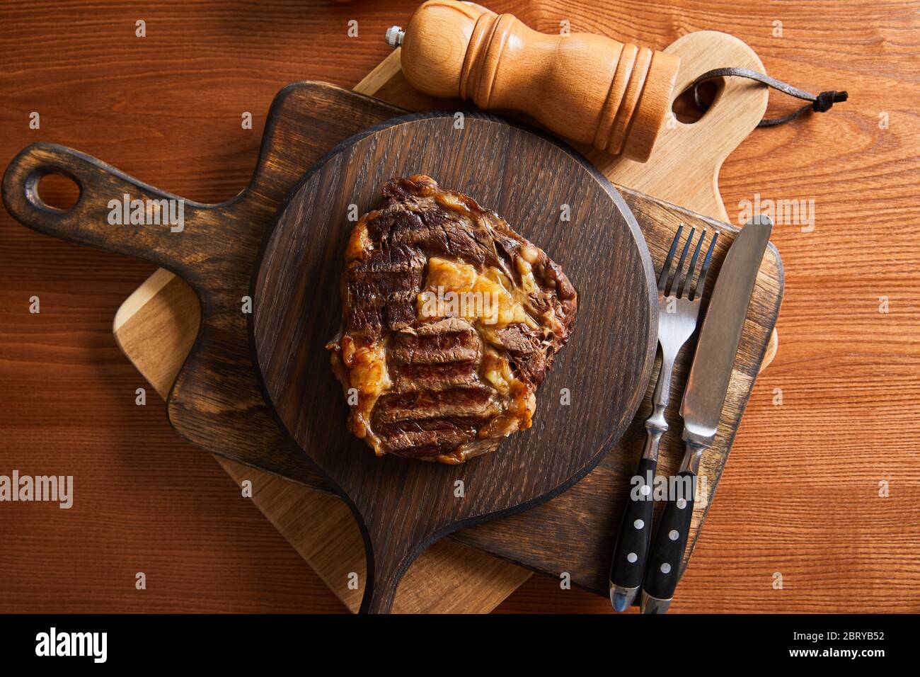 top view of tasty grilled steak served on wooden boards with cutlery ...