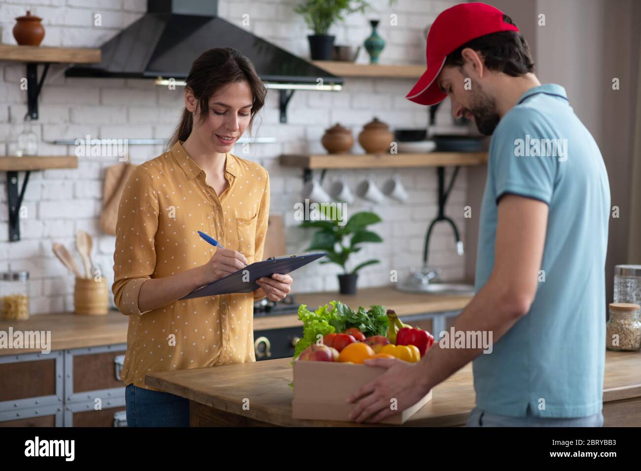 Woman receiving home food delivery from a courrier and signing a ...