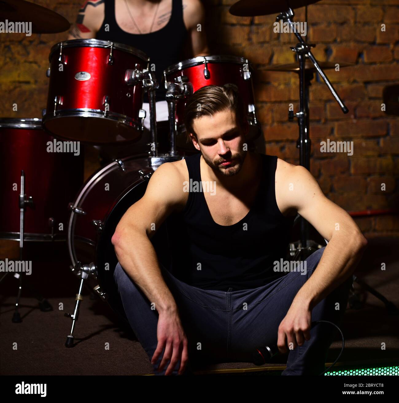 Singer with thoughtful face holds microphone sitting on scene. Pop ...