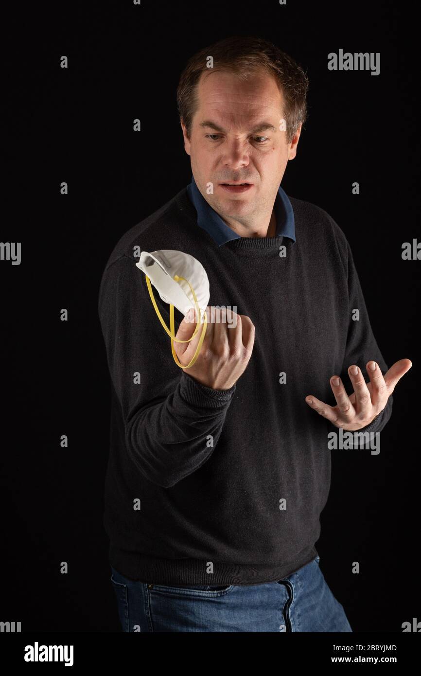A confused man holding a medical face mask, PPE Stock Photo - Alamy