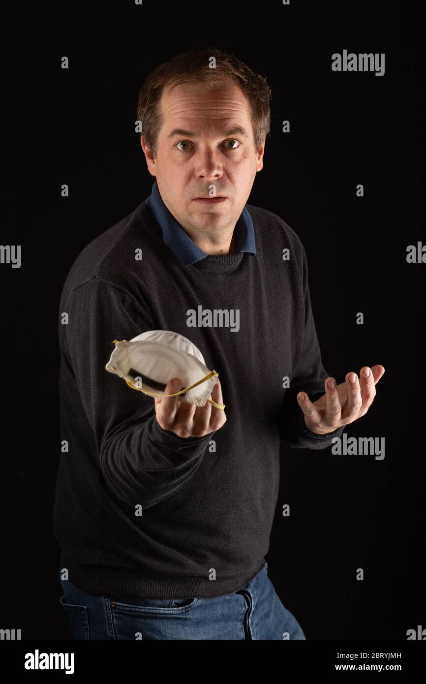 A confused man holding a medical face mask Stock Photo - Alamy