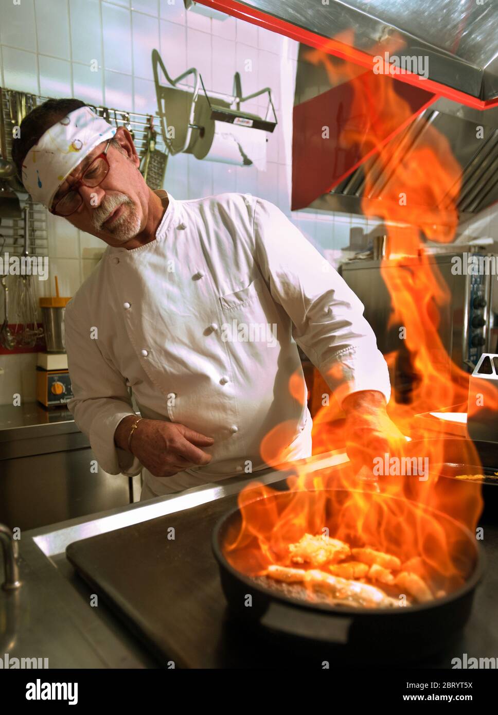 A chef in uniform working in a kitchen, flambeing the contents of a ...